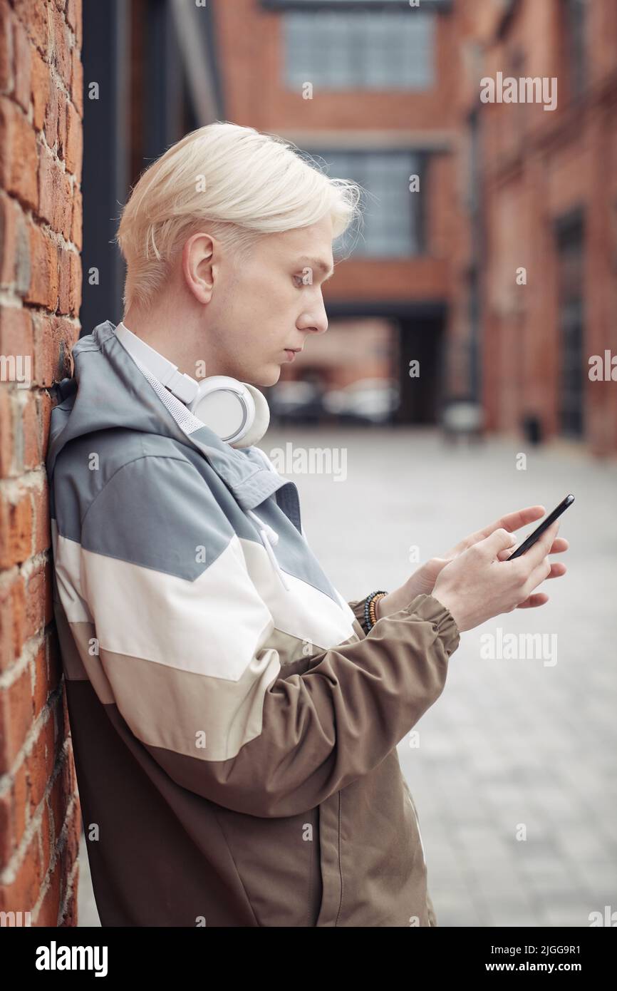 Blond guy with headphones on his neck scrolling through playlist in ...