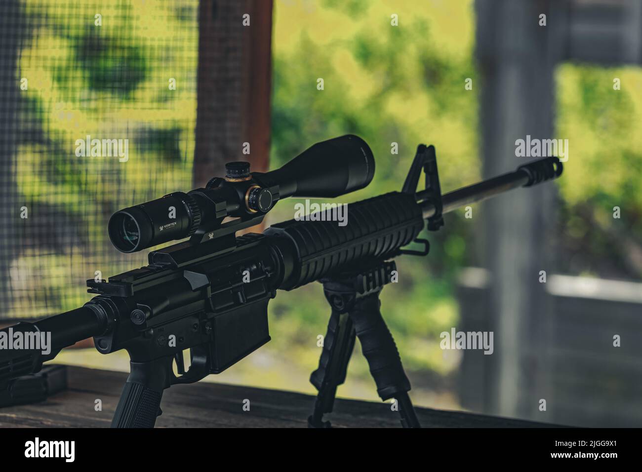 A closeup of a gun with an aim sight on stand near the window Stock ...