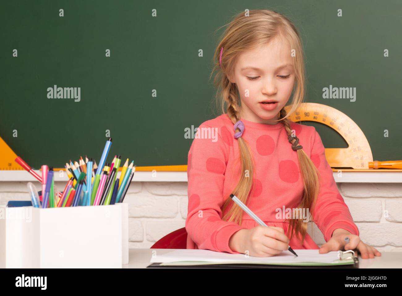 Child from elementary school sitting at table in classroom at primary ...