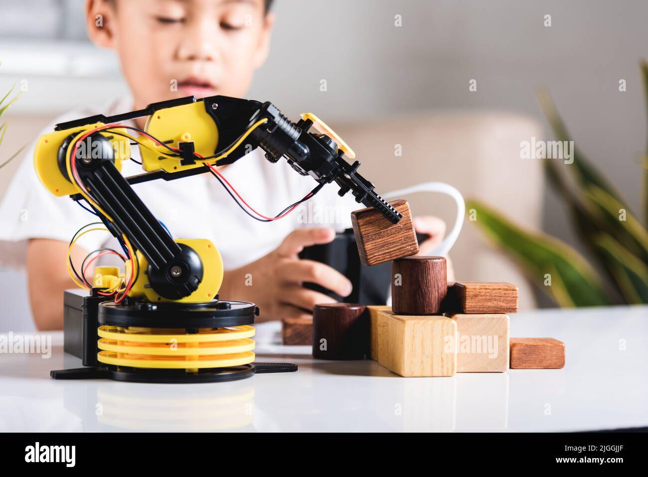 Happy Asian little boy using remote control playing robotic machine arm ...
