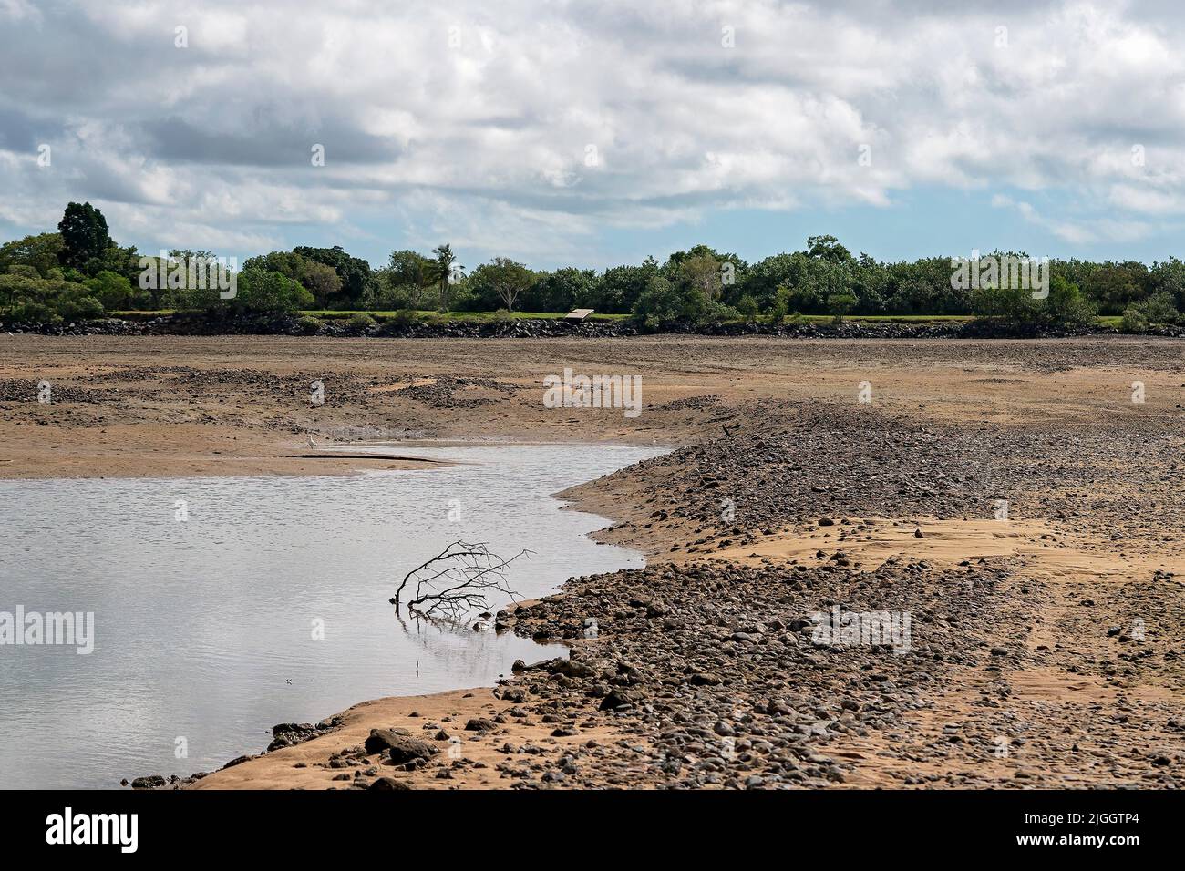 A gravel built up bank on the far side of a stony river bed at low tide ...