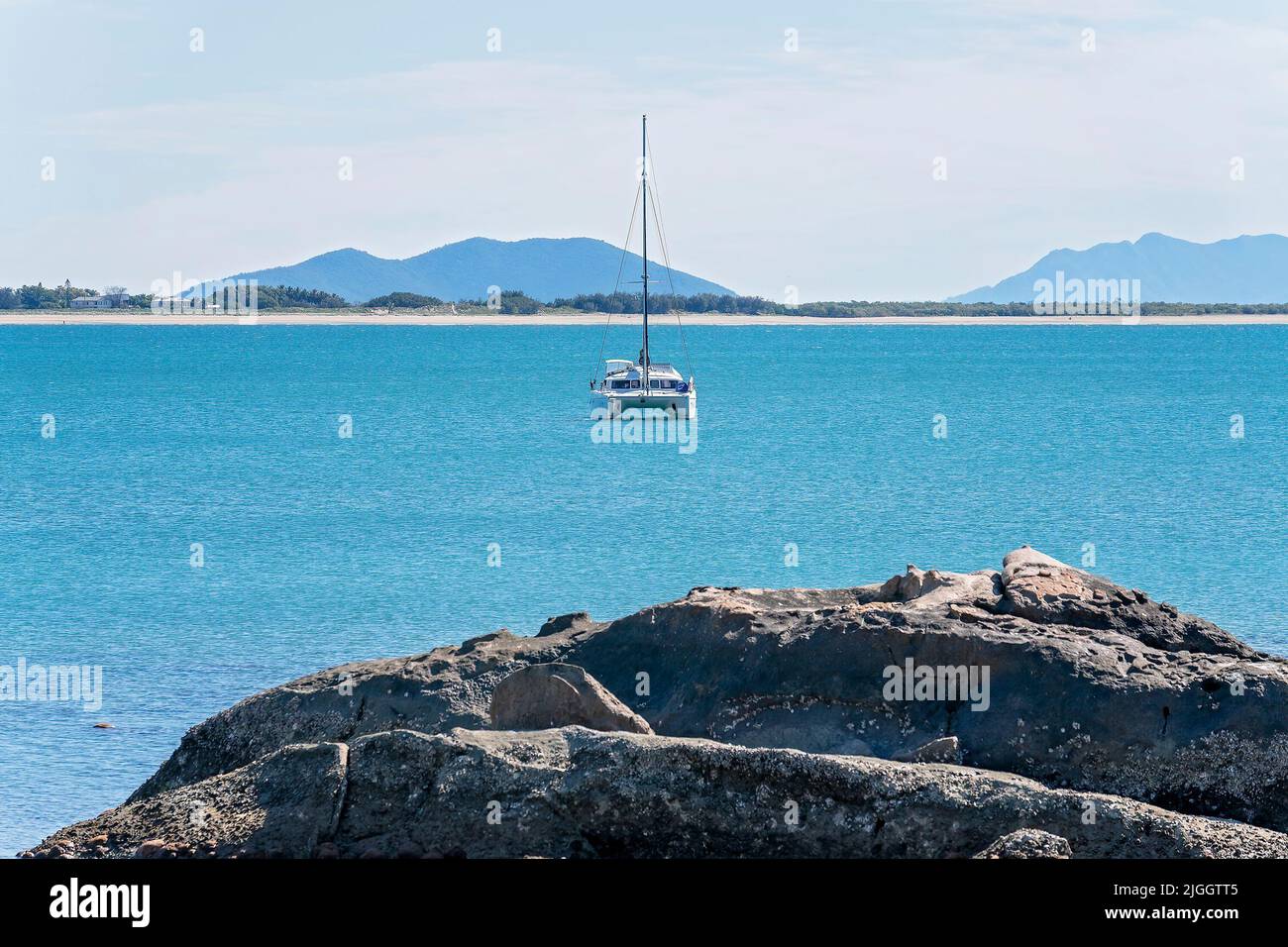 A luxury catamaran at anchor off shore from oyster covered rocks at ...