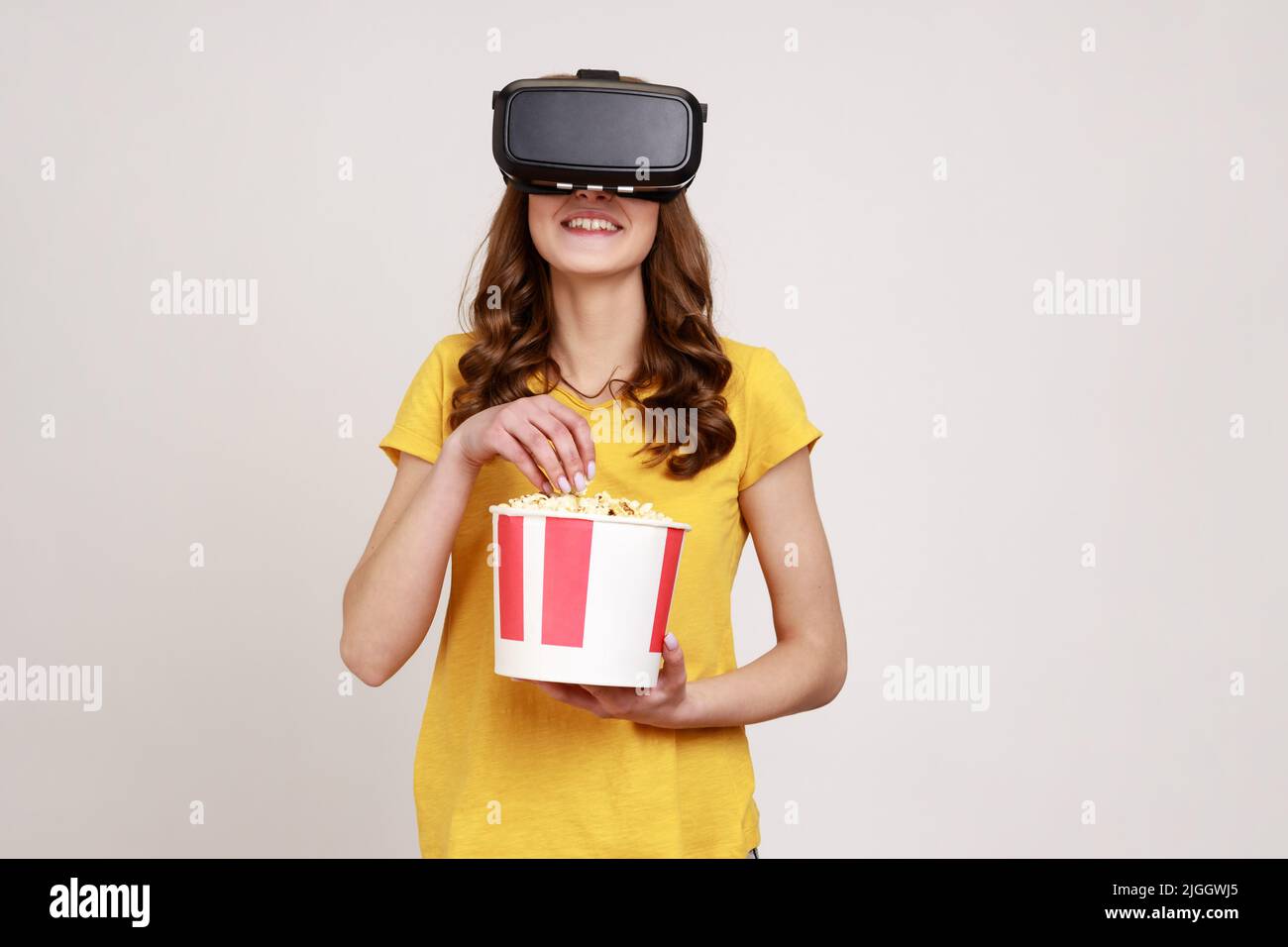Young smiling female in VR headset watching movie with popcorn, smiling ...