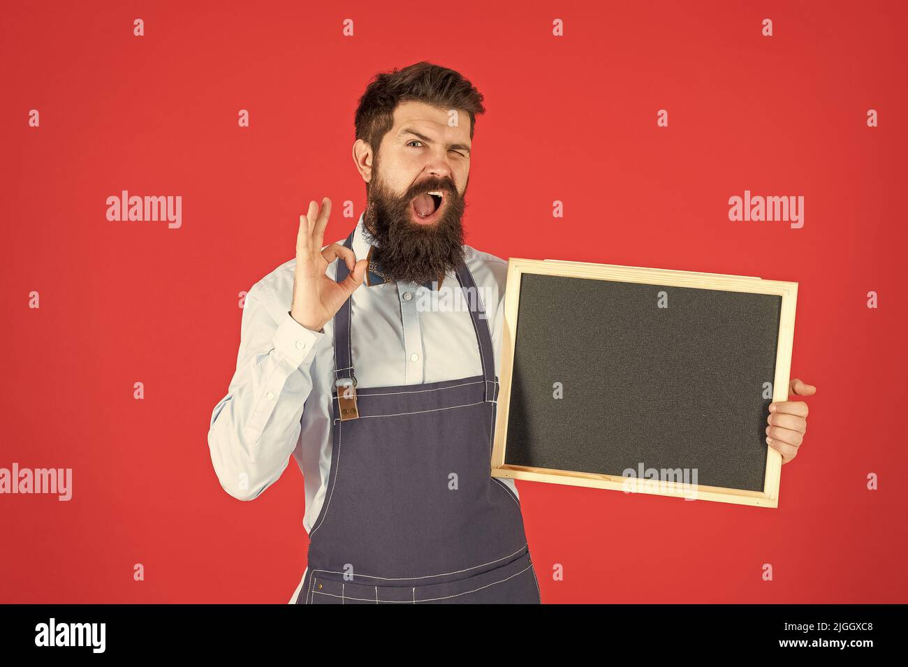 Happy winking man in barber apron hold school blackboard showing OK ...