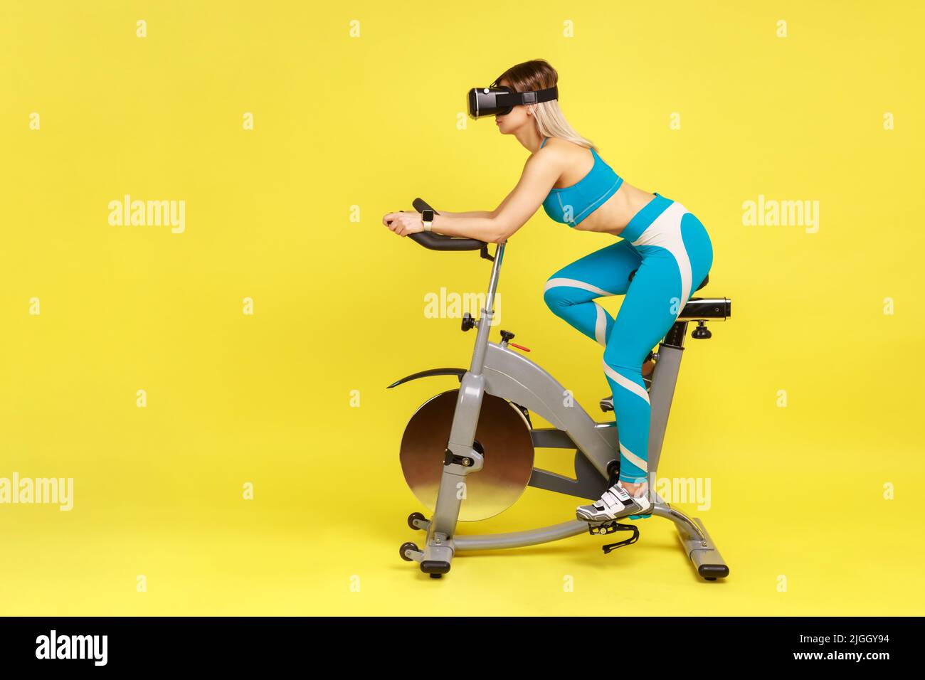 Side view portrait of slim woman riding exercise bike with virtual ...
