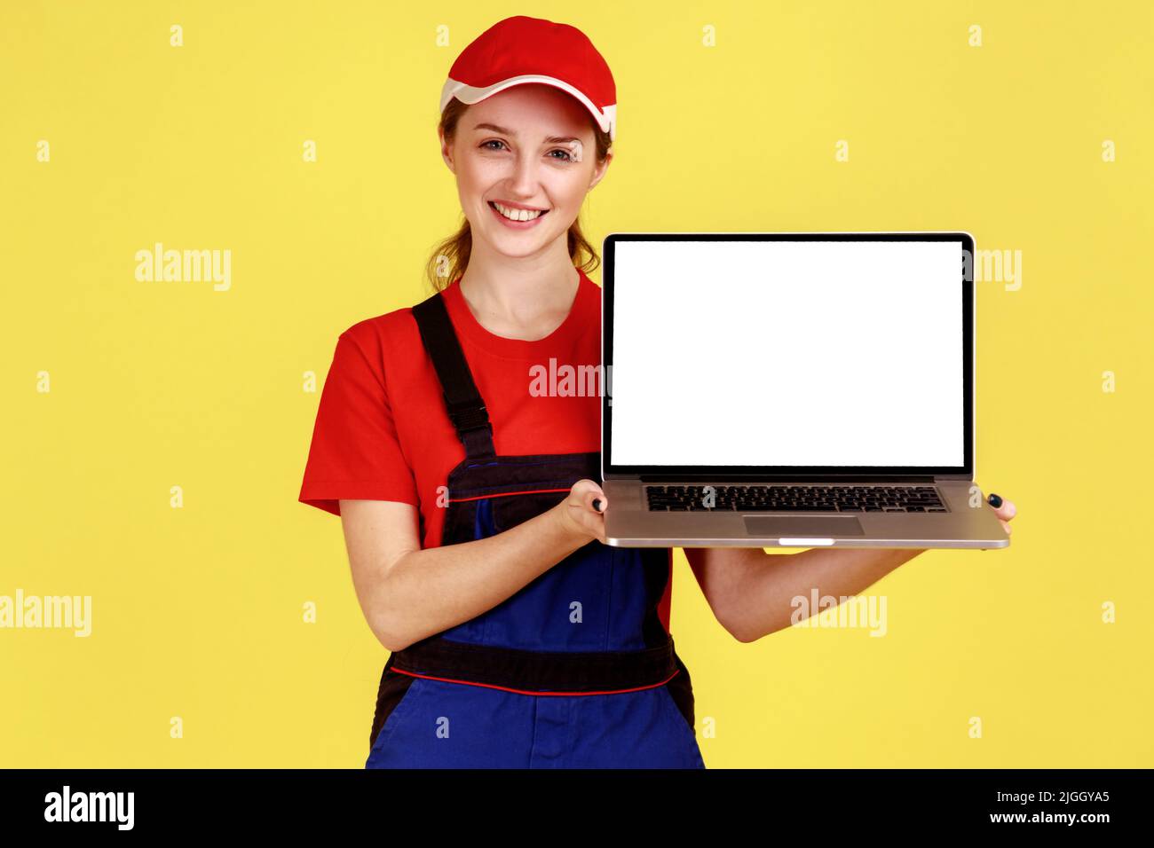 Portrait of smiling positive worker woman standing and showing laptop ...