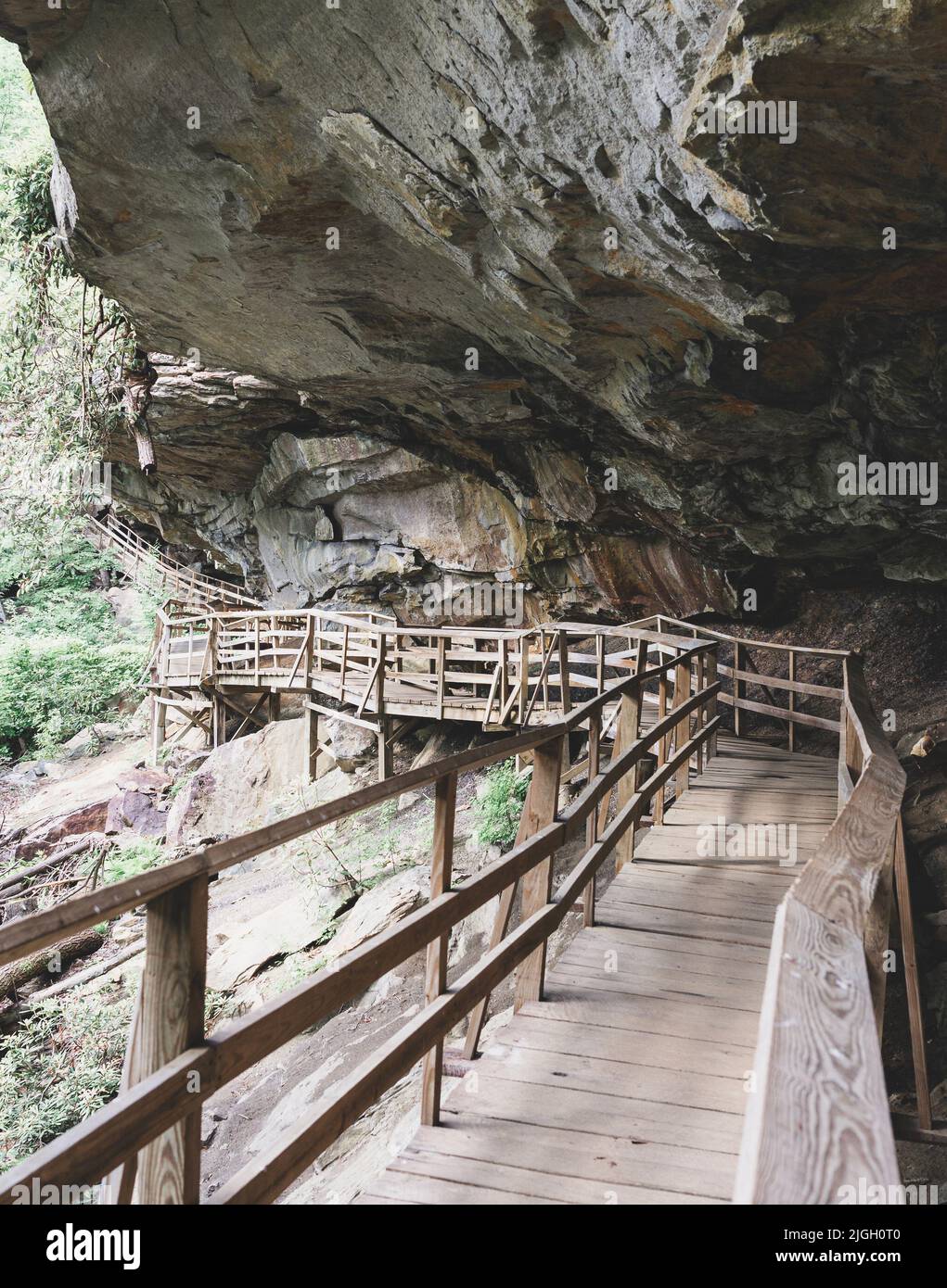A vertical shot of a wooden bridge under the rocky cliff in a rural ...
