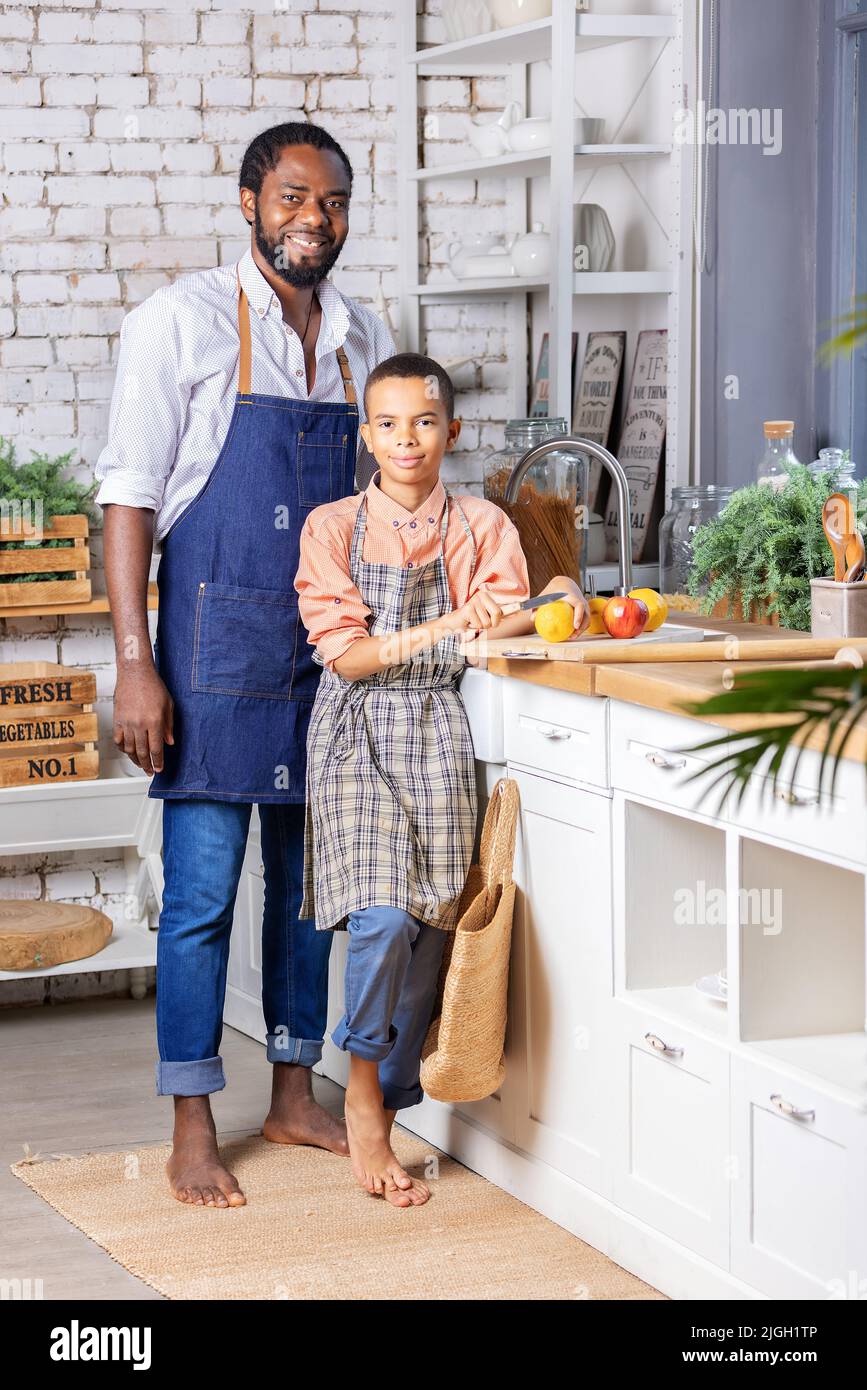 Black father and his son kid cooking fresh vegetables on kitchen at ...
