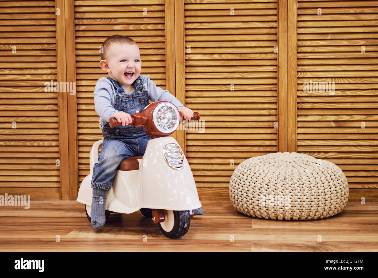 Happy baby boy rides a plastic children motorcycle in the playroom. A ...