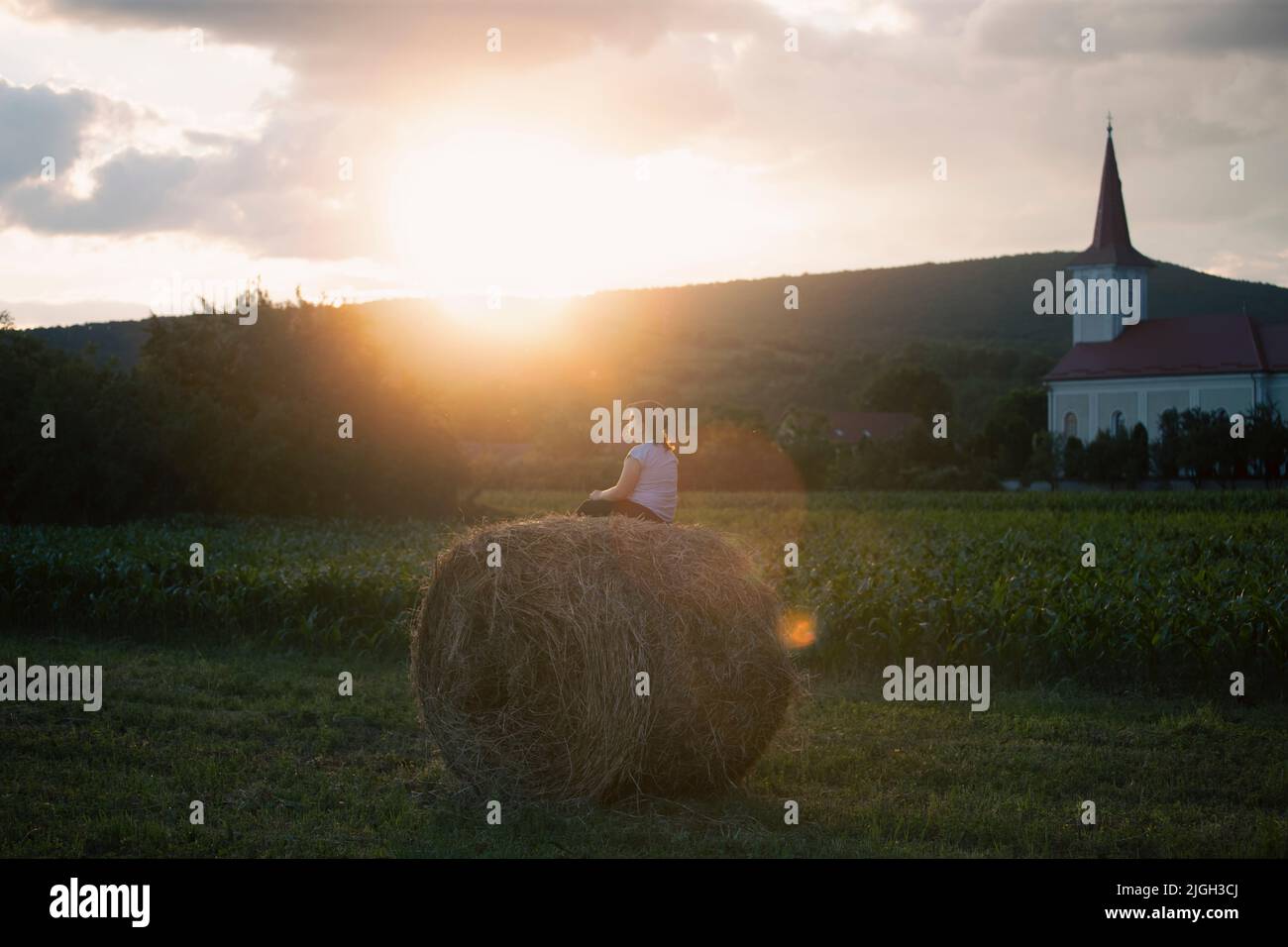 Caucasian girl having fun sitting on top of a golden hay bale on summer ...