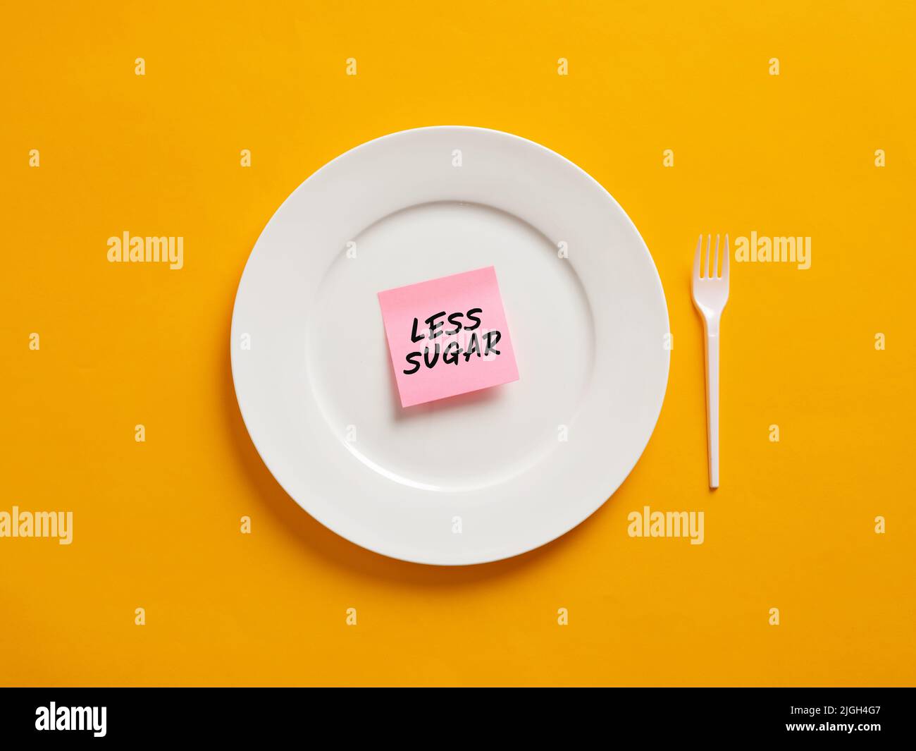 Notepaper with the word less sugar on a white plate. Less sugar intake ...