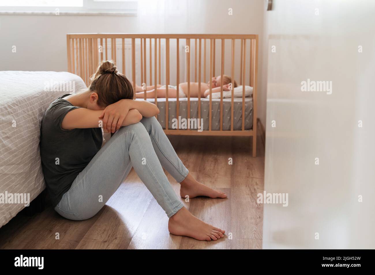Young mother suffering postnatal depression sitting on floor next to ...