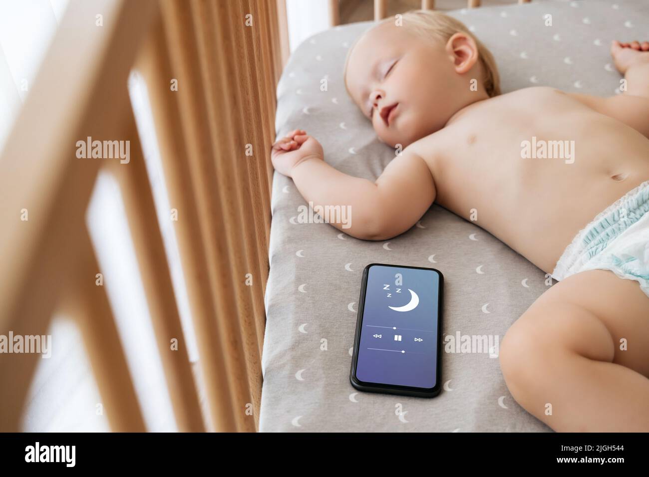 Little child in diaper napping in bed with phone playing lullaby in ...