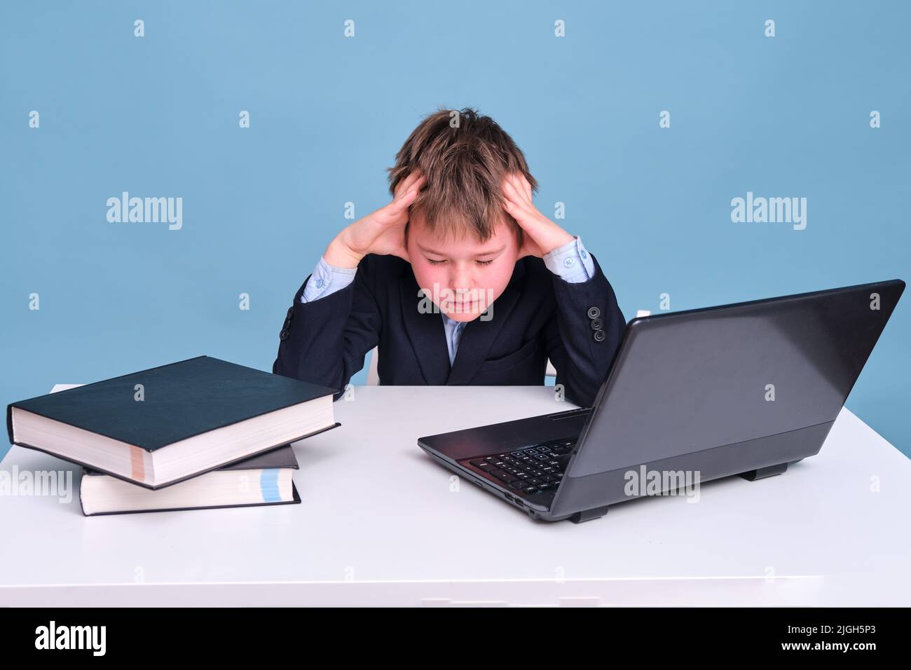 A sad boy in a school suit on distance learning, copy space on a blue ...