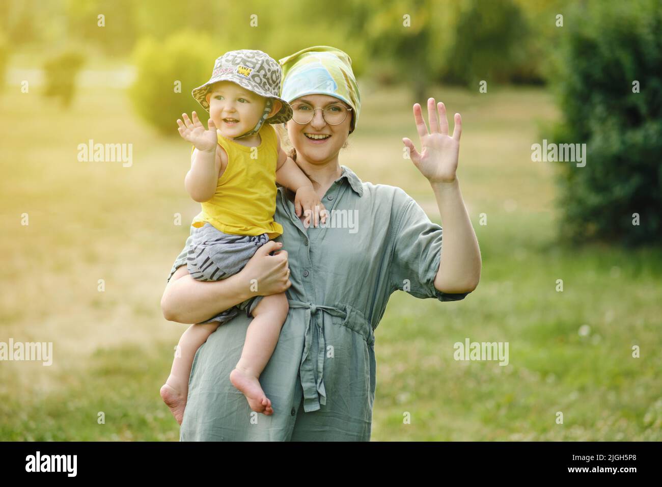 Mother holds a happy toddler baby boy in her arms and waves her hand ...