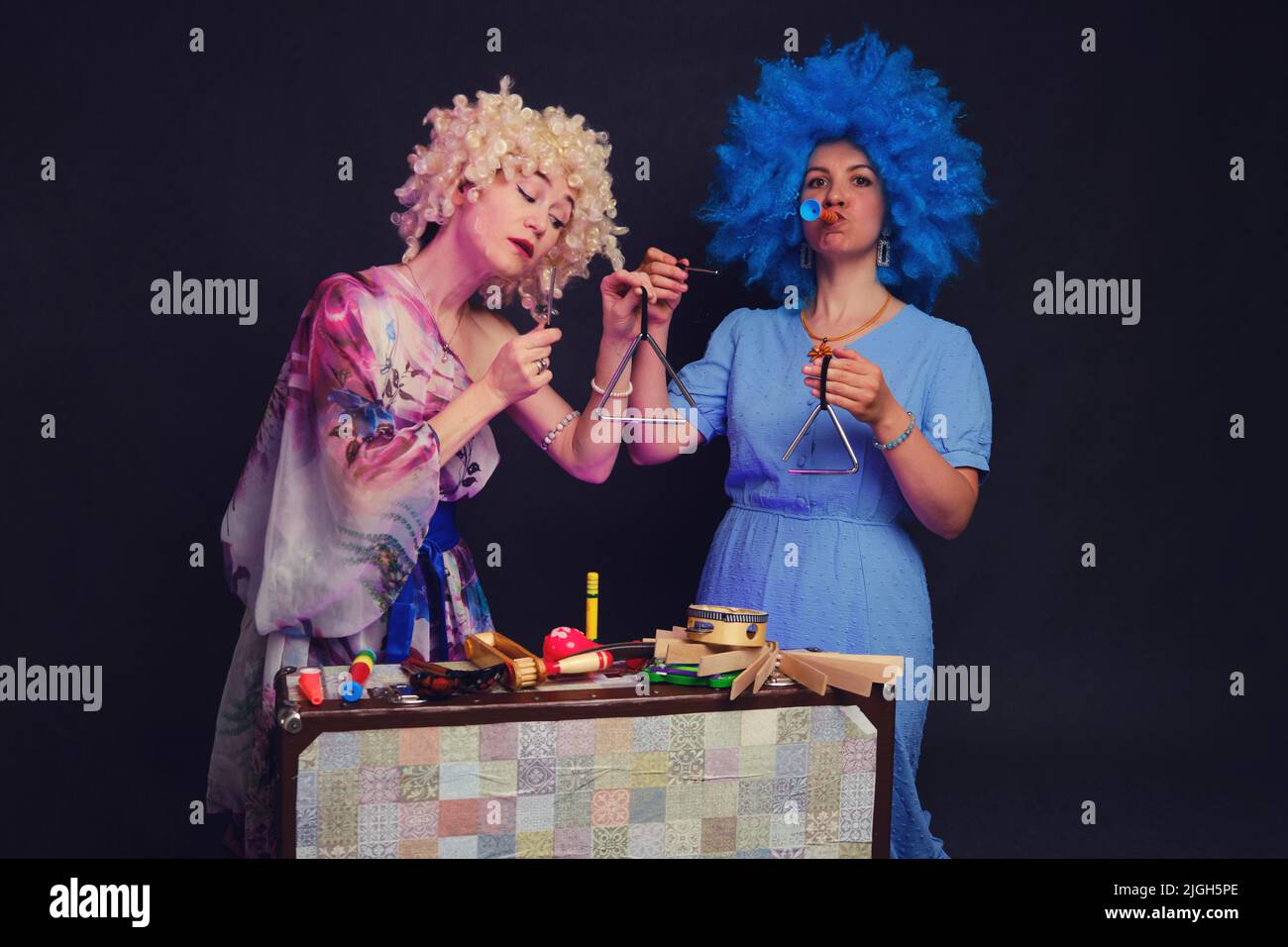 Happy women in funny wigs give a musical performance on a studio black ...