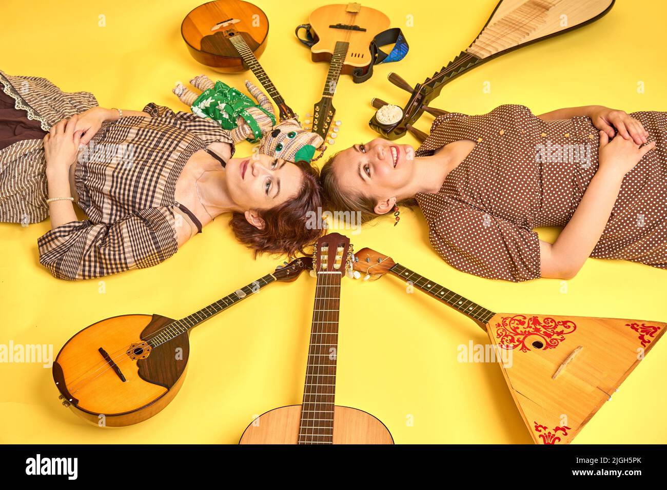 Women musicians in dresses with musical instruments on a yellow studio ...