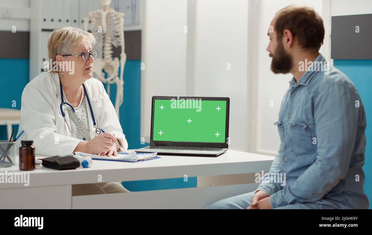 Senior doctor and patient looking at laptop with greenscreen at checkup ...
