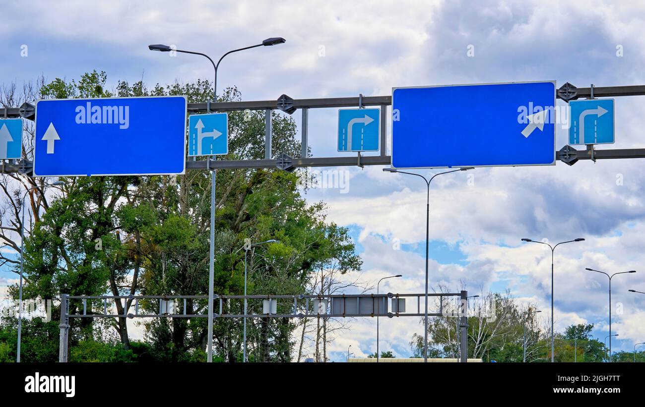 Blue pointing empty road signs with arrows and cloudy sky and trees ...
