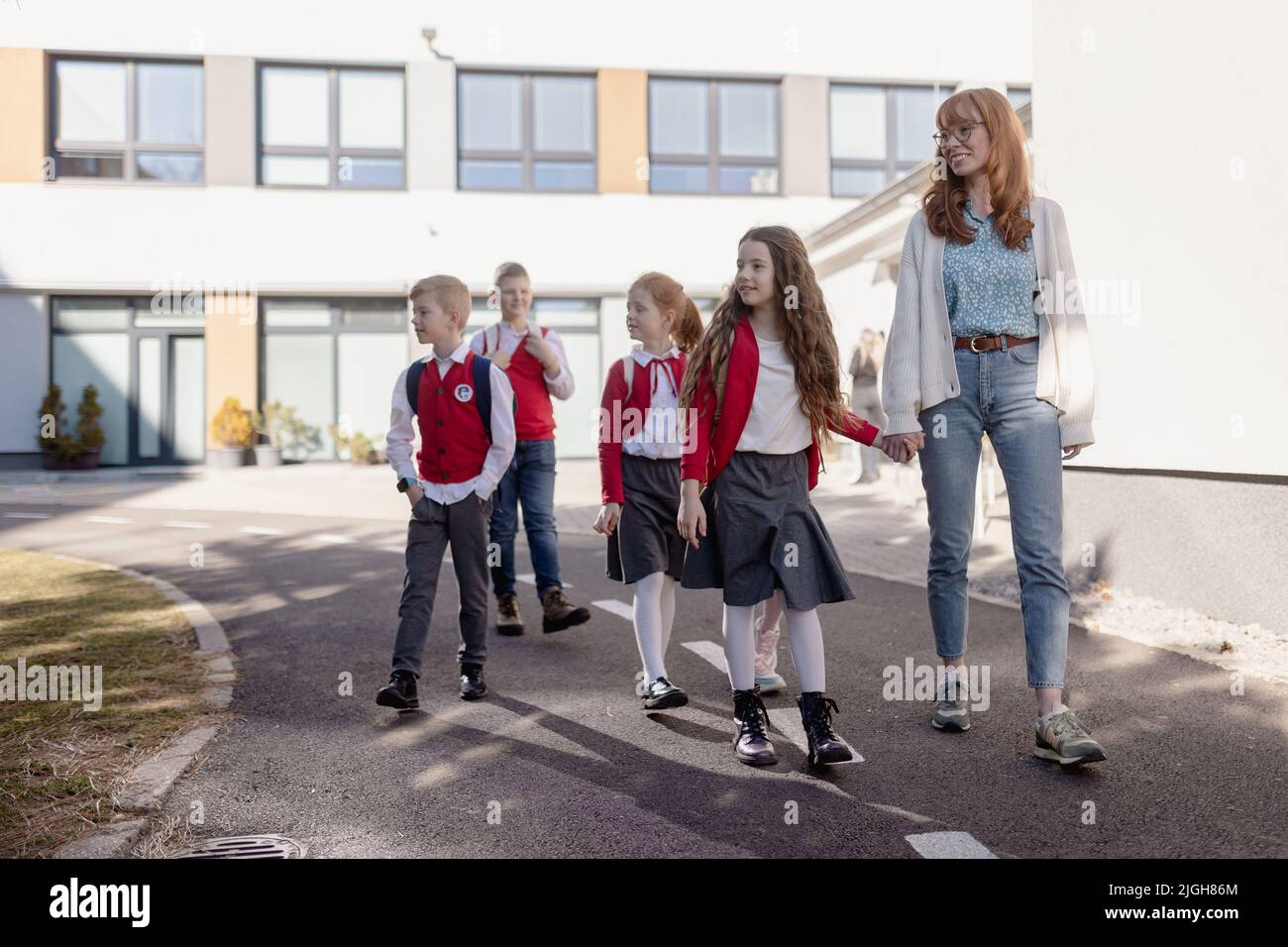 Happy schoolkids in uniforms with teacher walking at a schoolyard Stock ...
