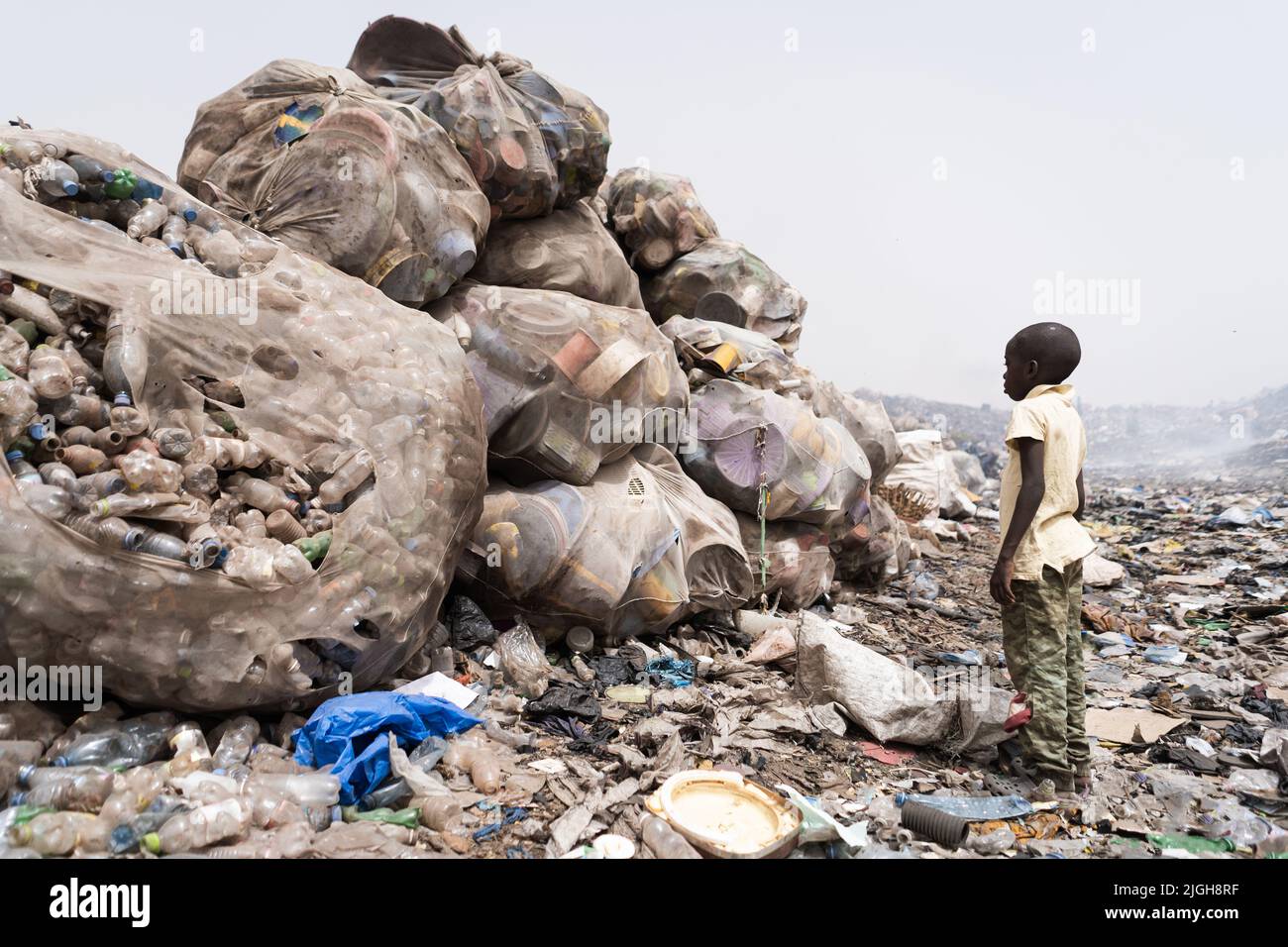 African child in a smoky landfill looking at giant bags with plastic ...