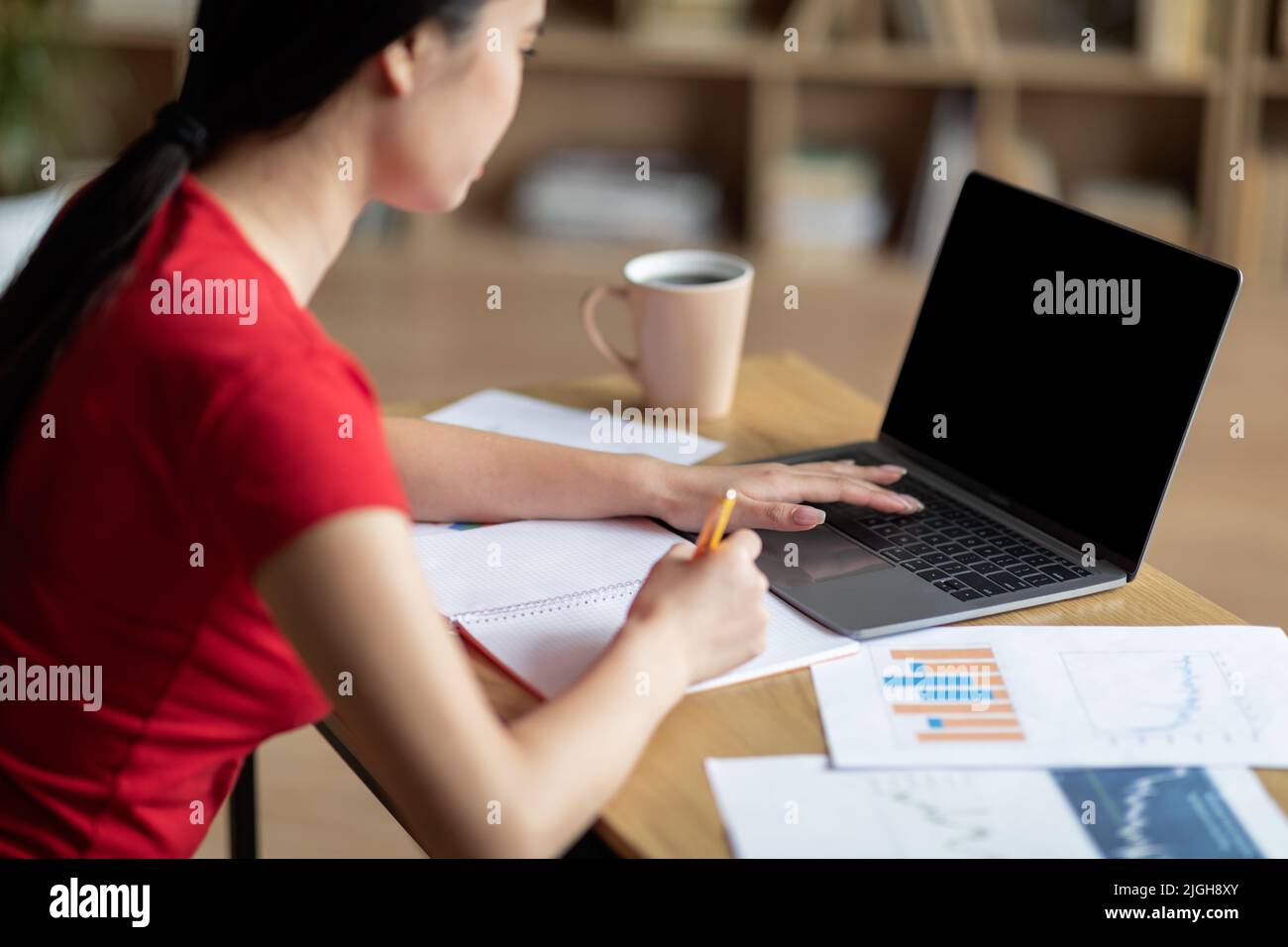 Busy concentrated teen asian lady study at table with laptop with empty ...