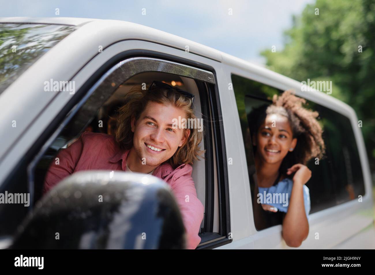 Multiracial young friends travelling together by car, looking through ...