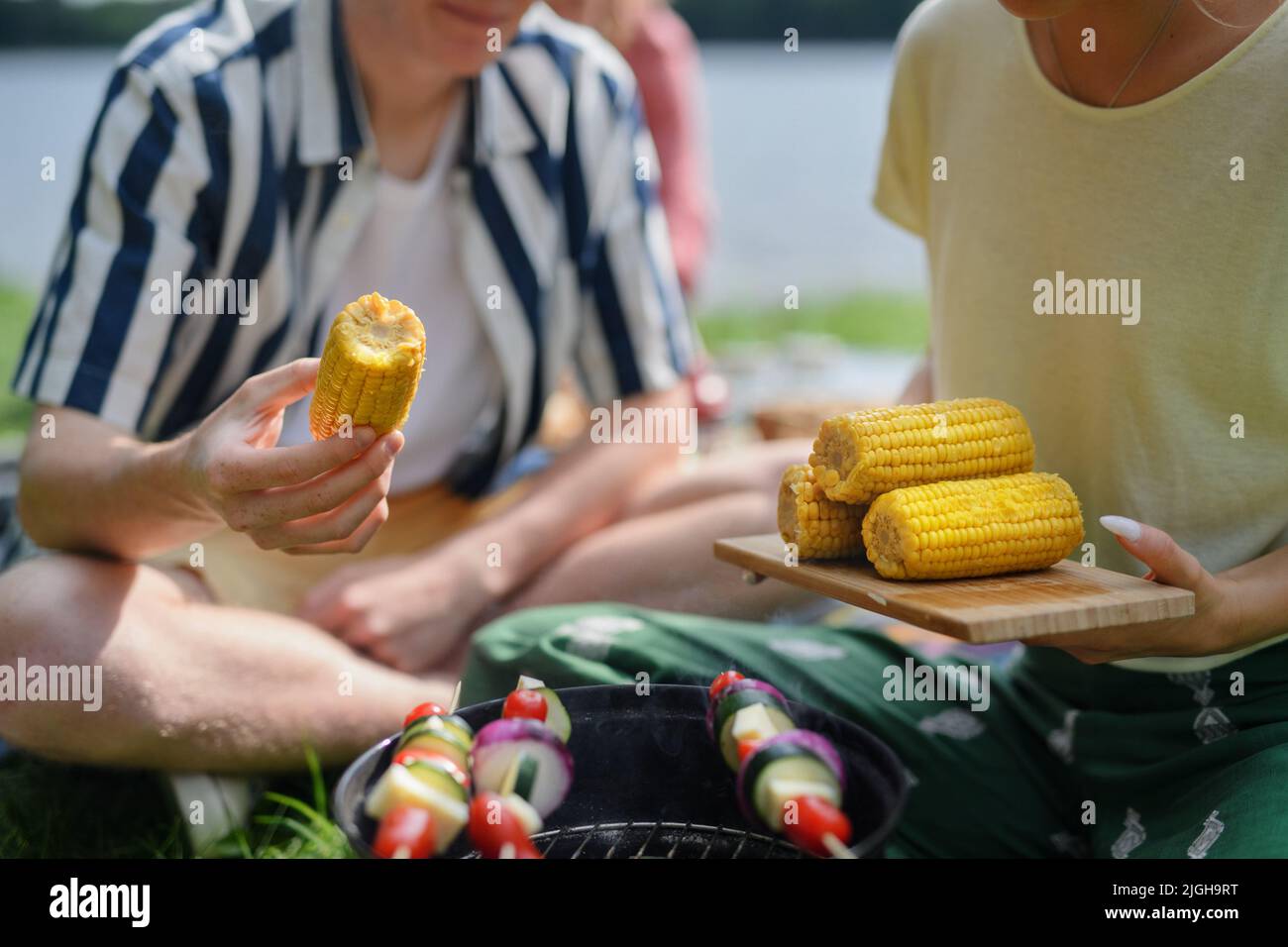 Close-up of young friends putting corn on grill and having barbecue ...