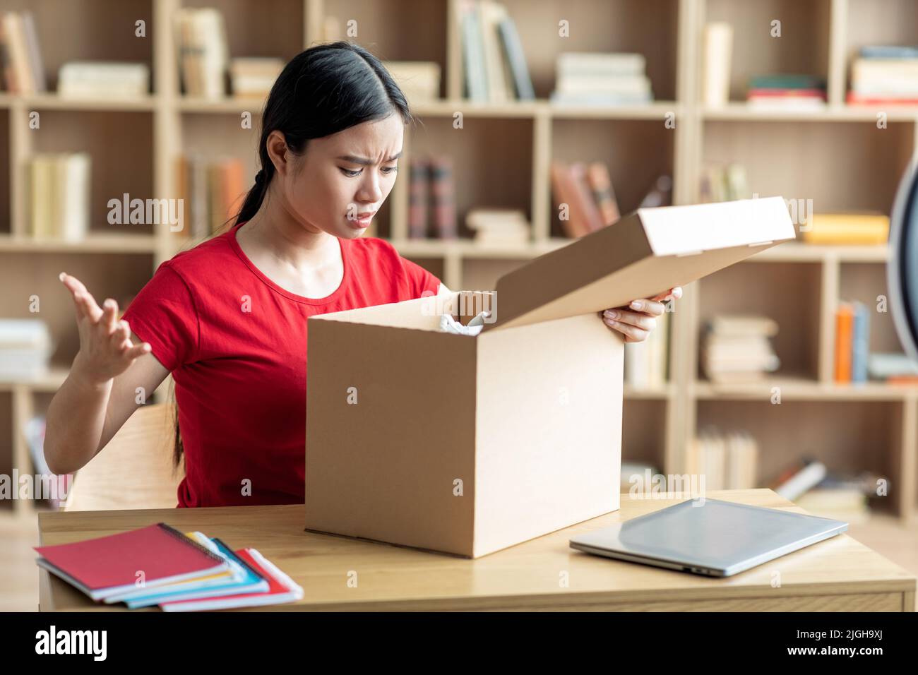 Frustrated disappointed young japanese lady opens cardboard box and sad ...