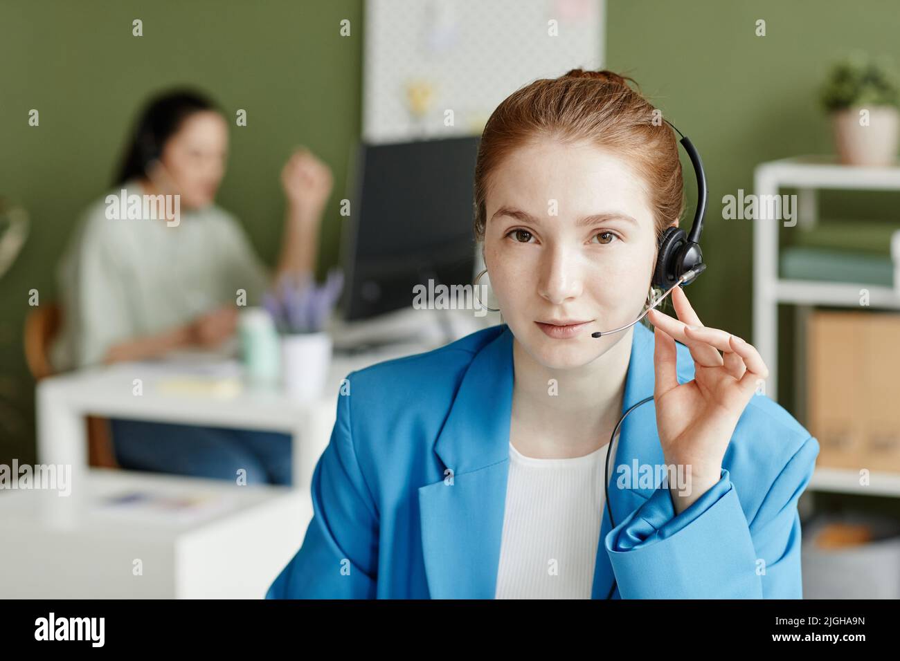 Portrait of young call centre operator in headphones looking at camera ...
