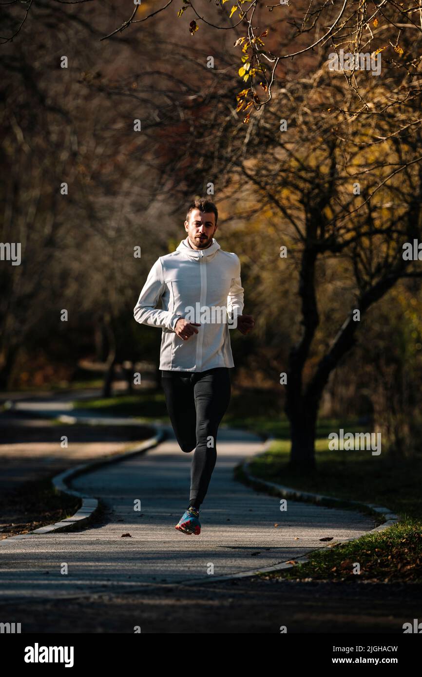 A vertical shot of a young active male with a white jacket jogging on a ...