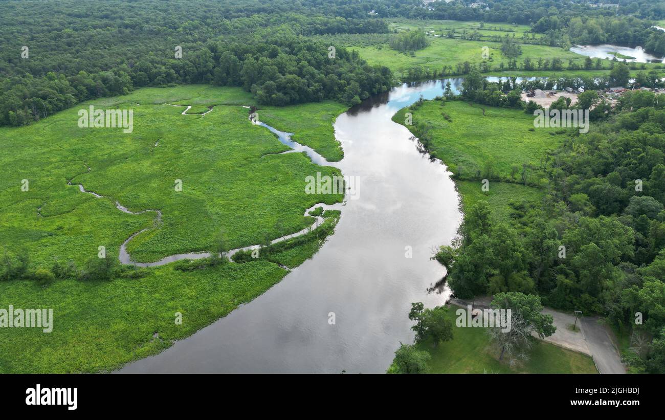 An aerial view of a narrow river passing through fields with forests ...