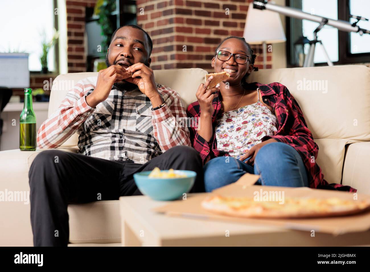 Young man and woman eating slice of pizza and drinking bottles of beer ...