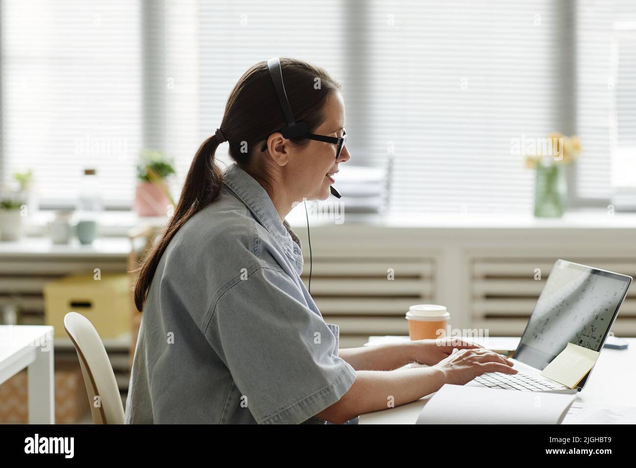 Young woman in headphones communicating online with customer using ...