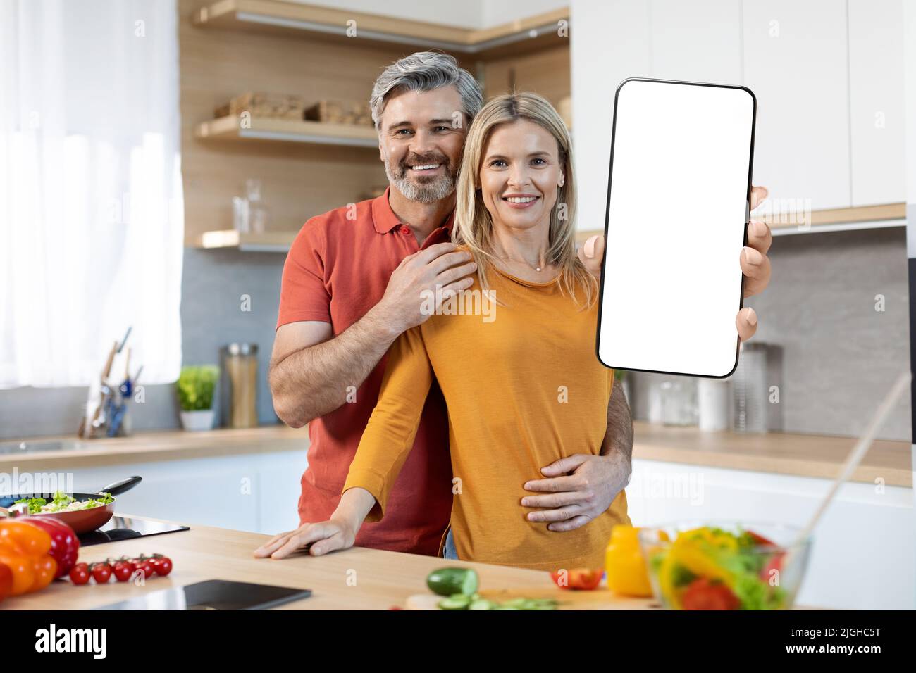Loving spouses cooking together, showing smartphone, mockup Stock Photo ...