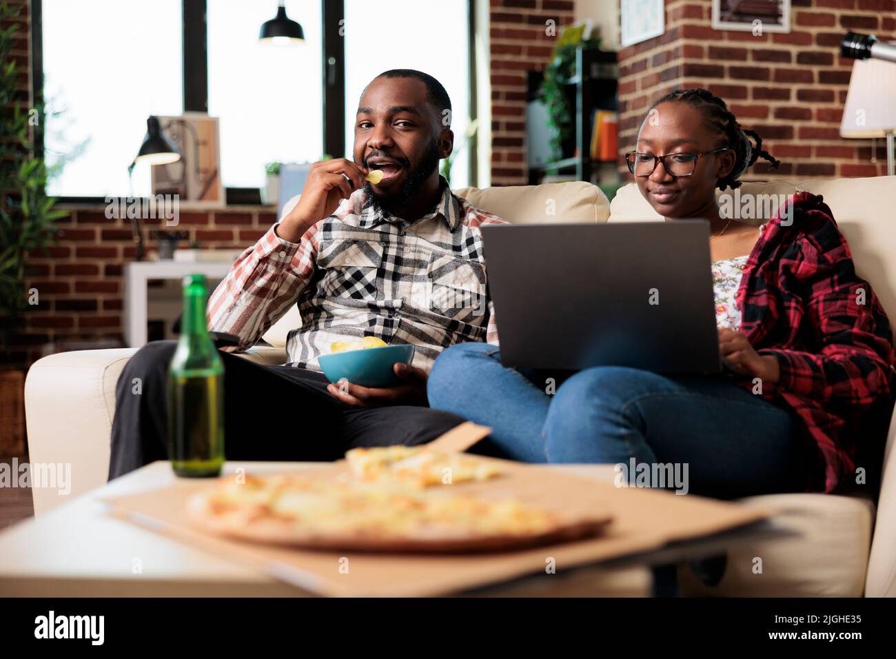 African american couple eating chips and using laptop in front of ...