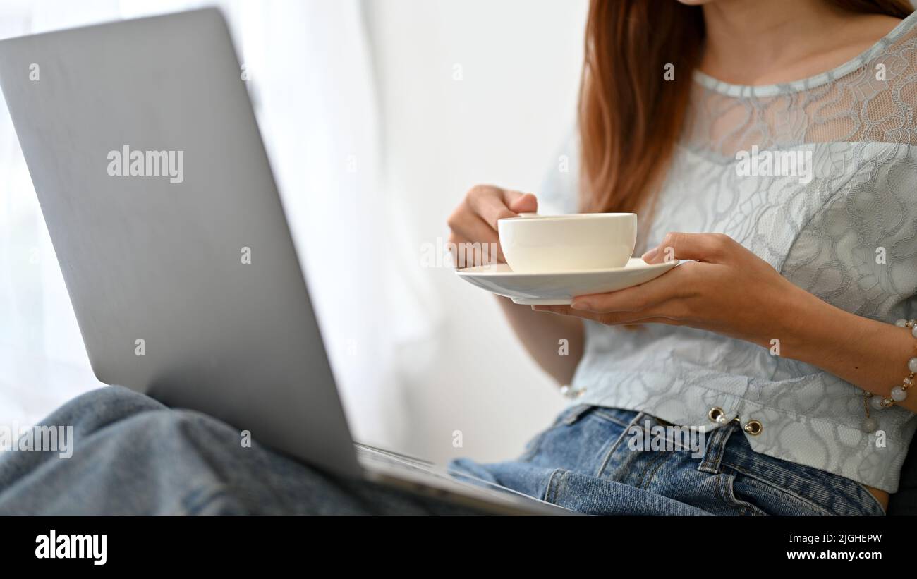 Attractive young Asian female using laptop computer while sipping a hot ...