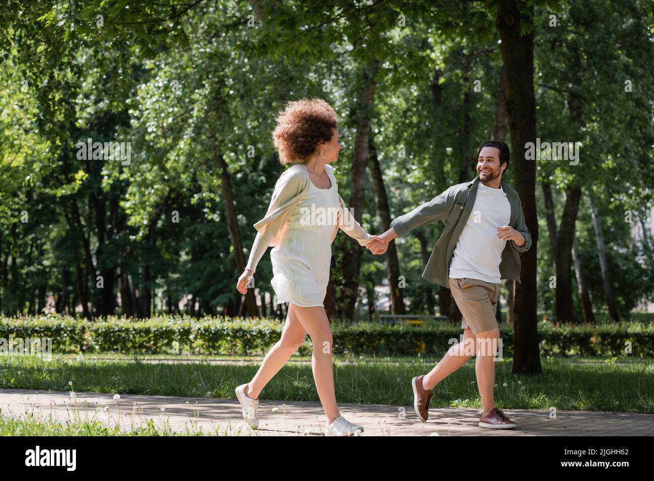 full length of positive young couple holding hands while running ...