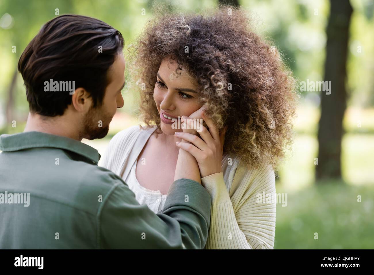 tender man touching cheek of happy and curly woman in green park Stock ...