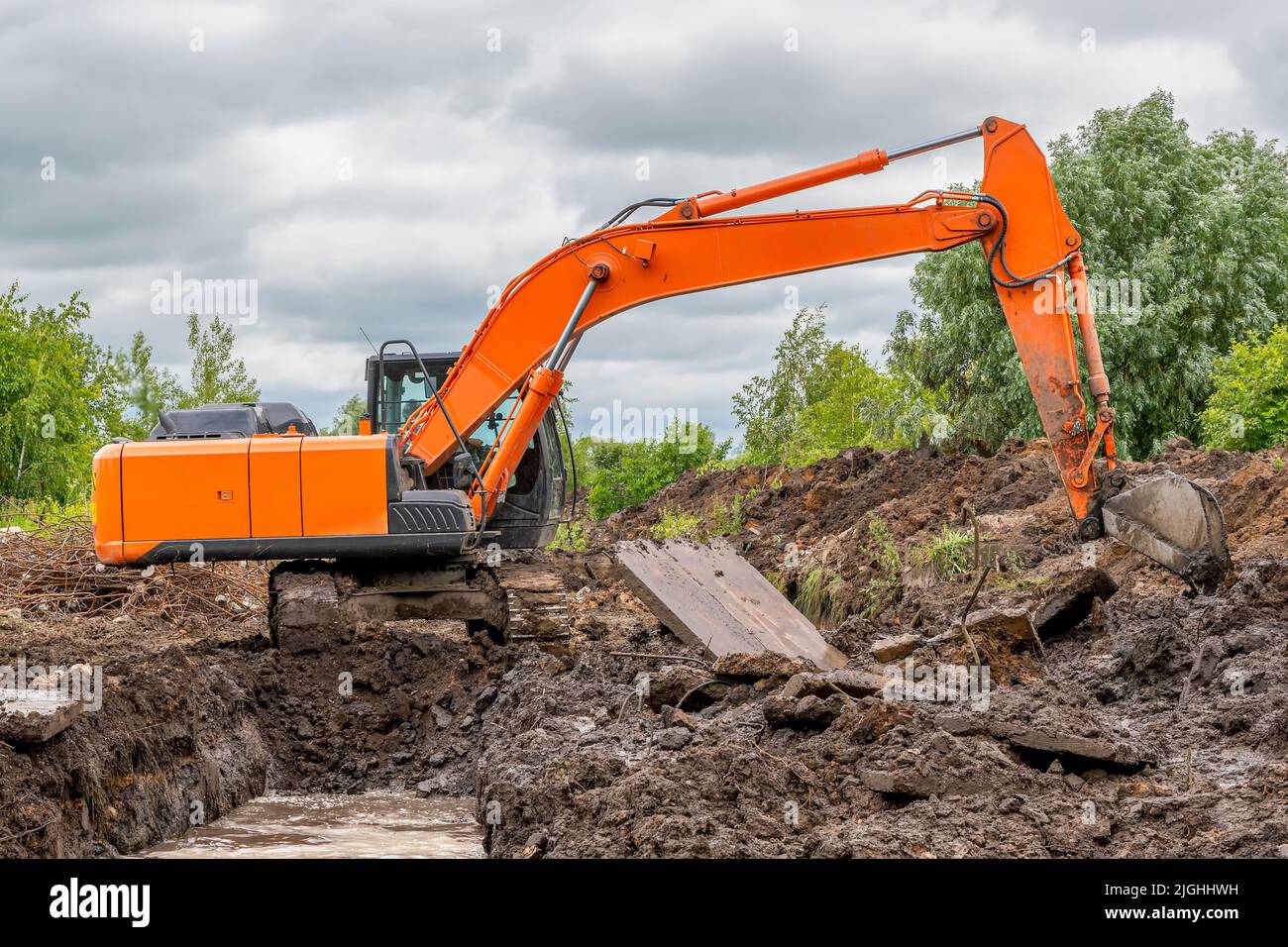 Large orange crawler excavator is excavating (digging a trench) against ...