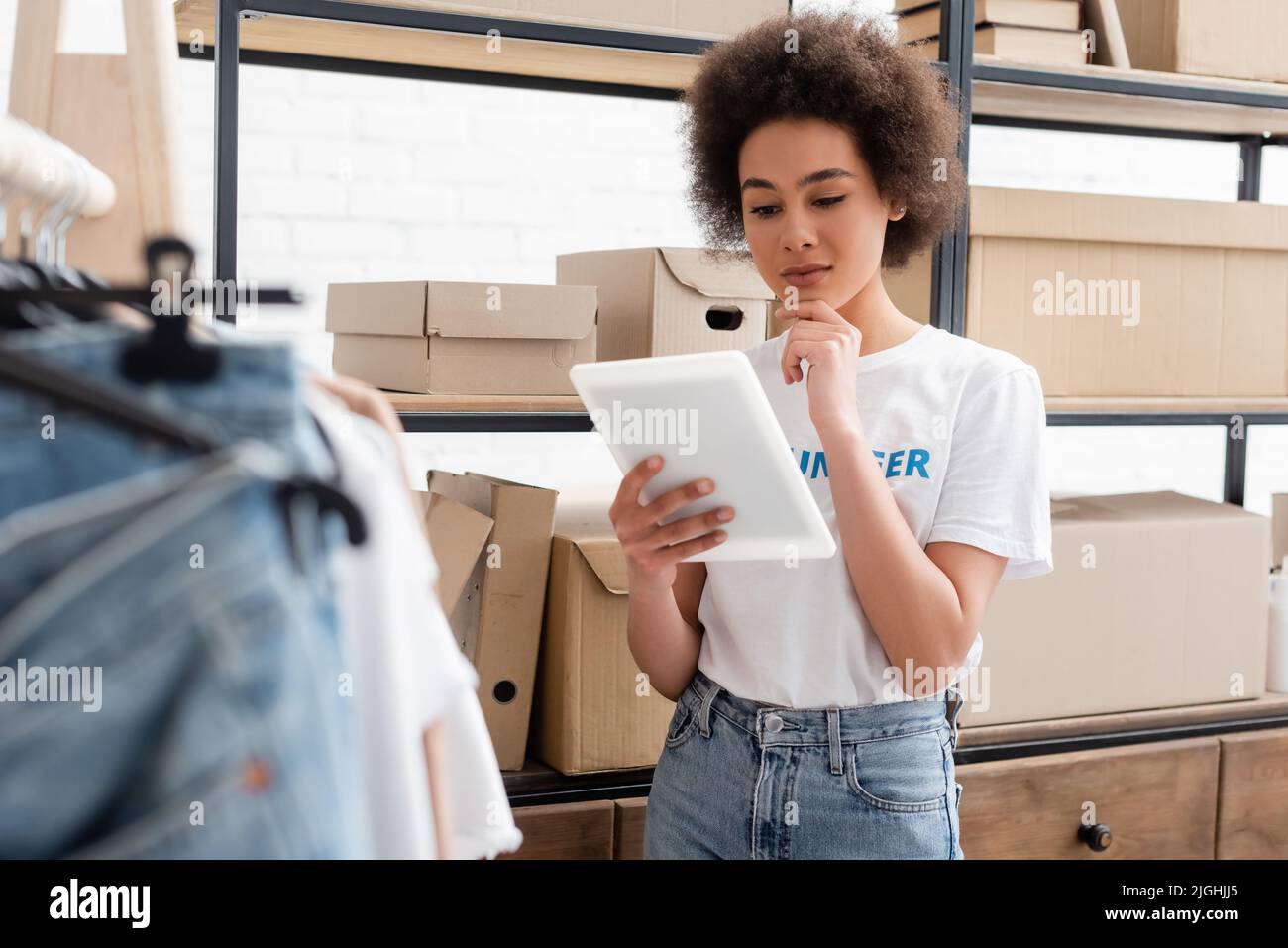 pensive african american volunteer looking at digital tablet near rack ...