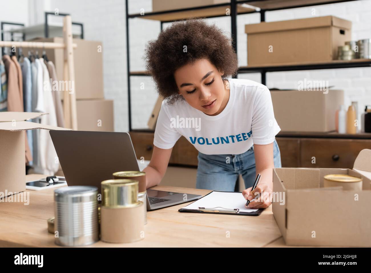 young african american volunteer writing on clipboard near laptop in ...
