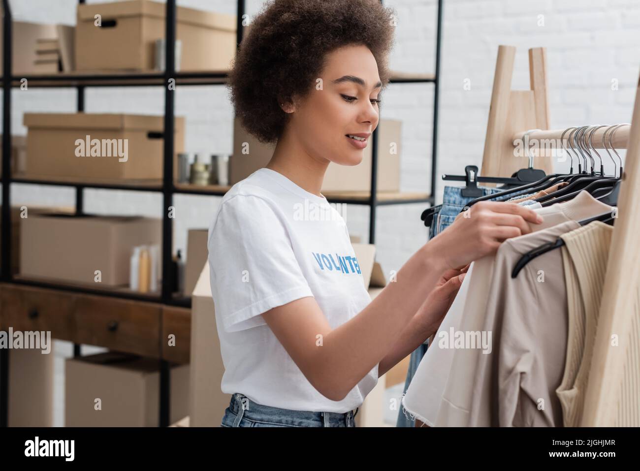 smiling african american volunteer sorting clothing in charity center ...