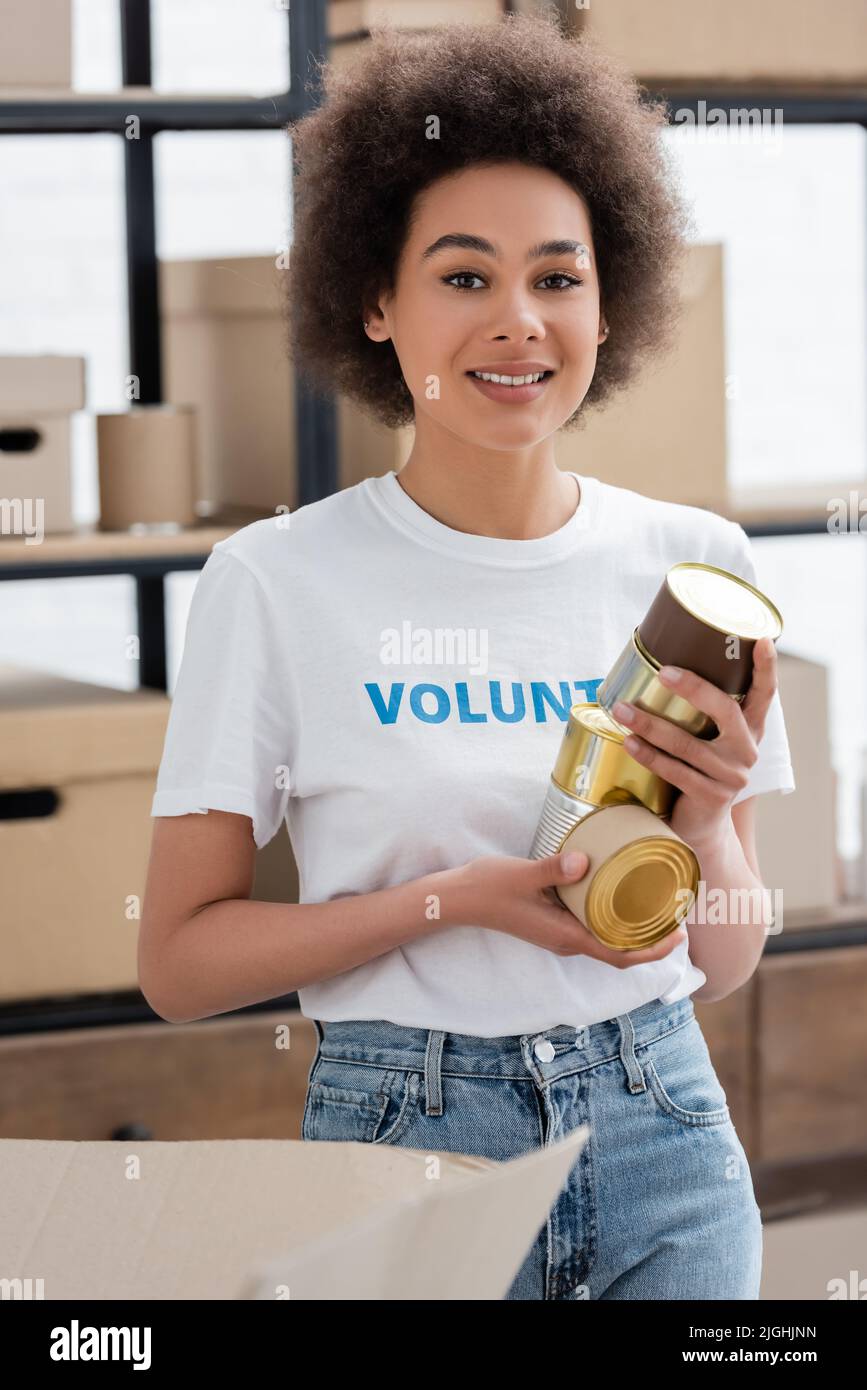 young african american woman with canned food smiling at camera in ...