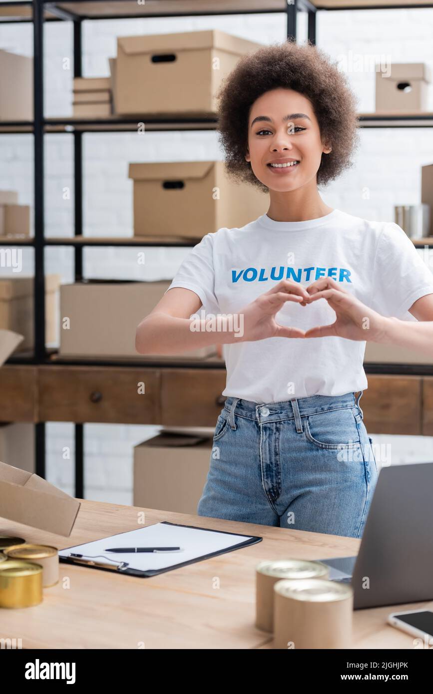 happy african american volunteer showing heart sign near clipboard on ...