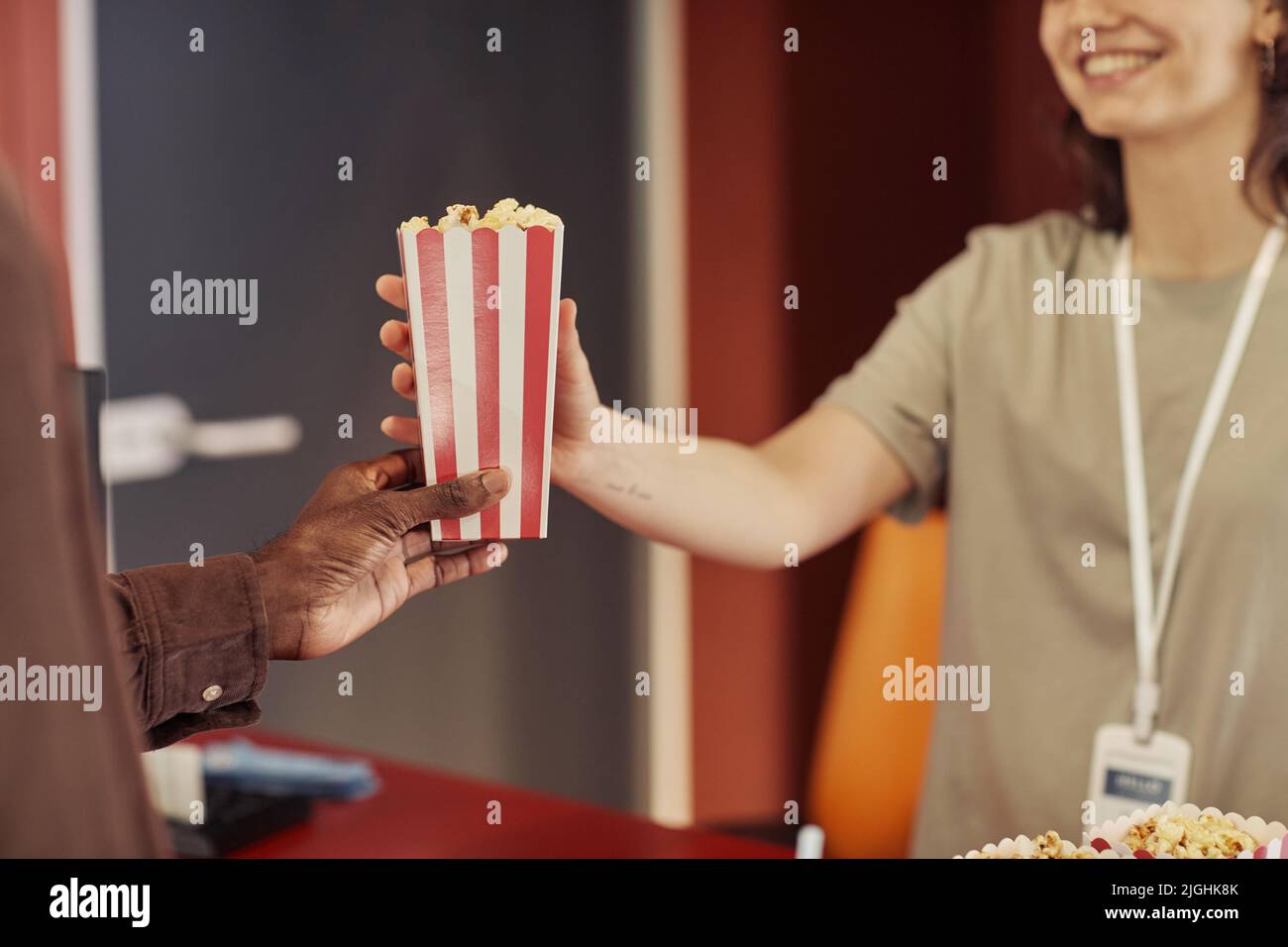 Close-up of young smiling seller selling popcorn to customer at counter ...