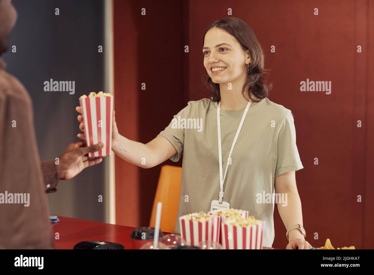 Young smiling woman selling popcorn at counter to the customer before ...