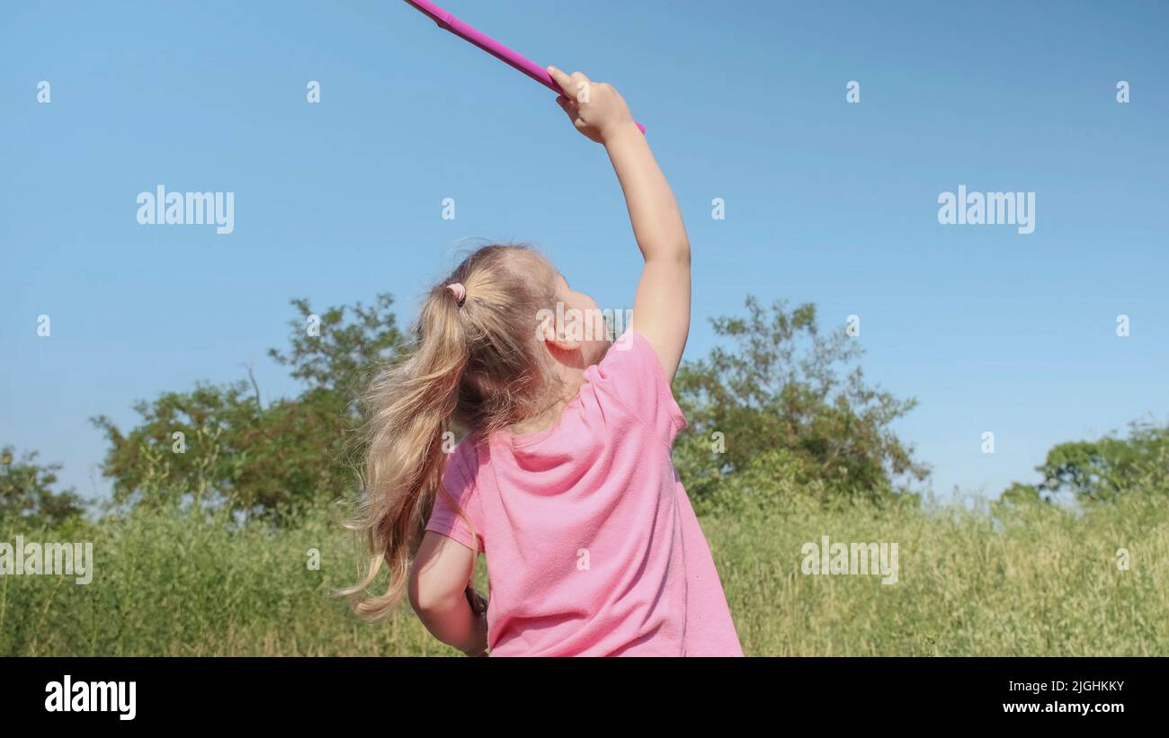 Little girl plays with butterfly net of tall grass in city park. Cute ...