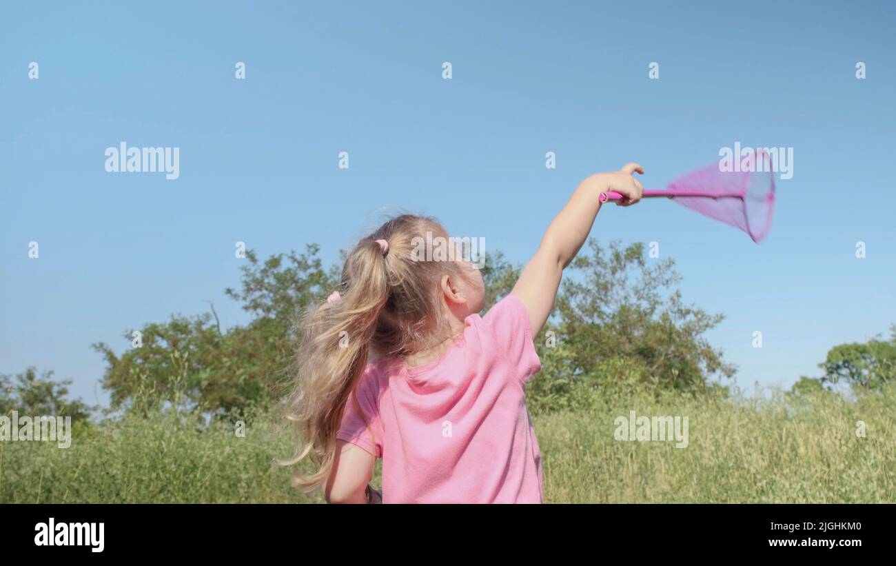 Little girl plays with butterfly net of tall grass in city park. Cute ...