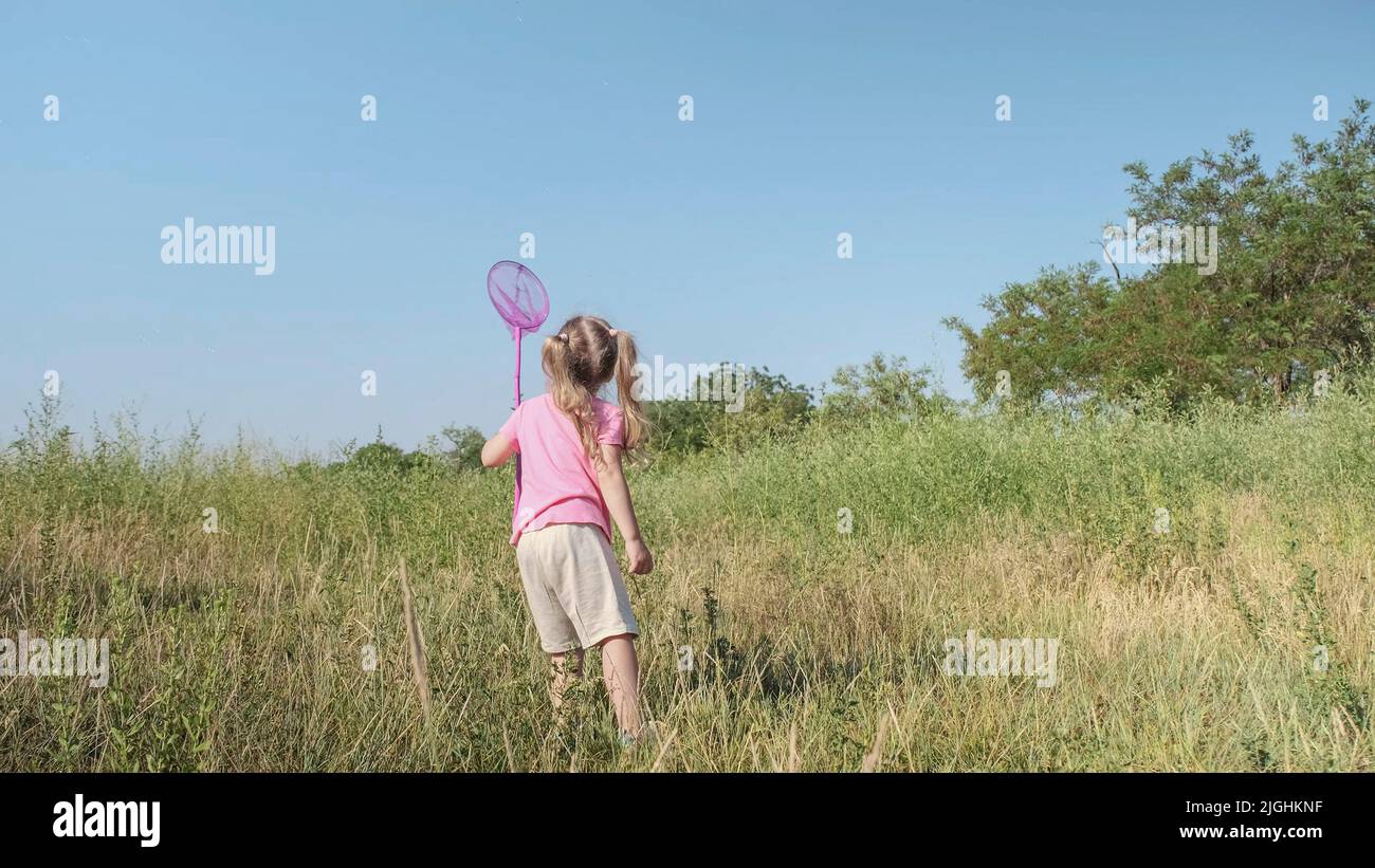 Little girl plays with butterfly net of tall grass in city park. Cute ...